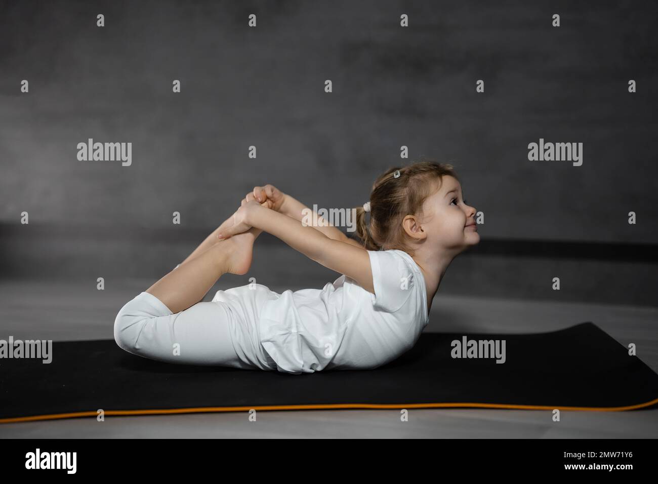 Little cute girl practicing yoga pose on grey background in dark room ...