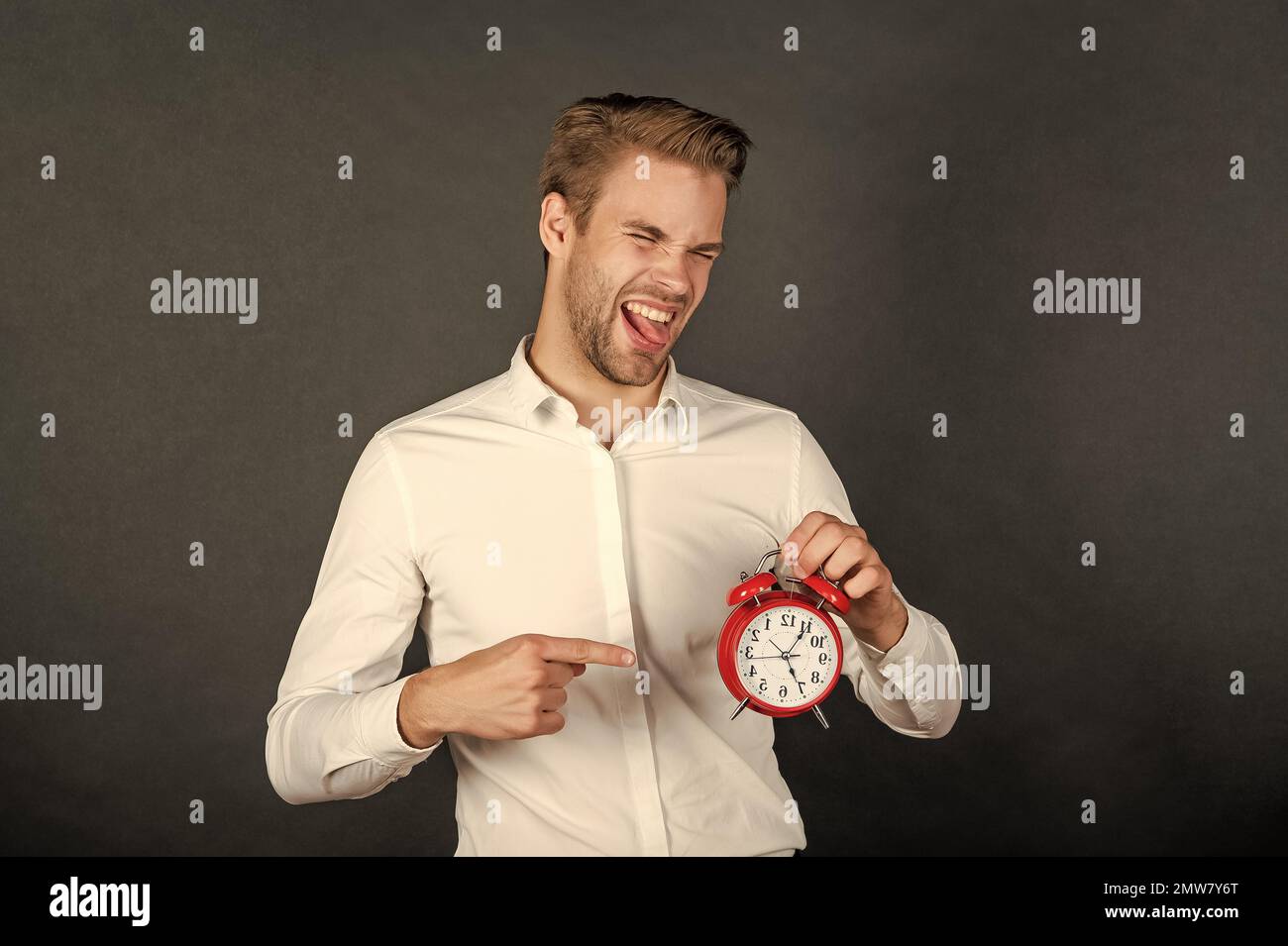 Happy crazy guy sticking tongue while pointing finger at alarm clock ...