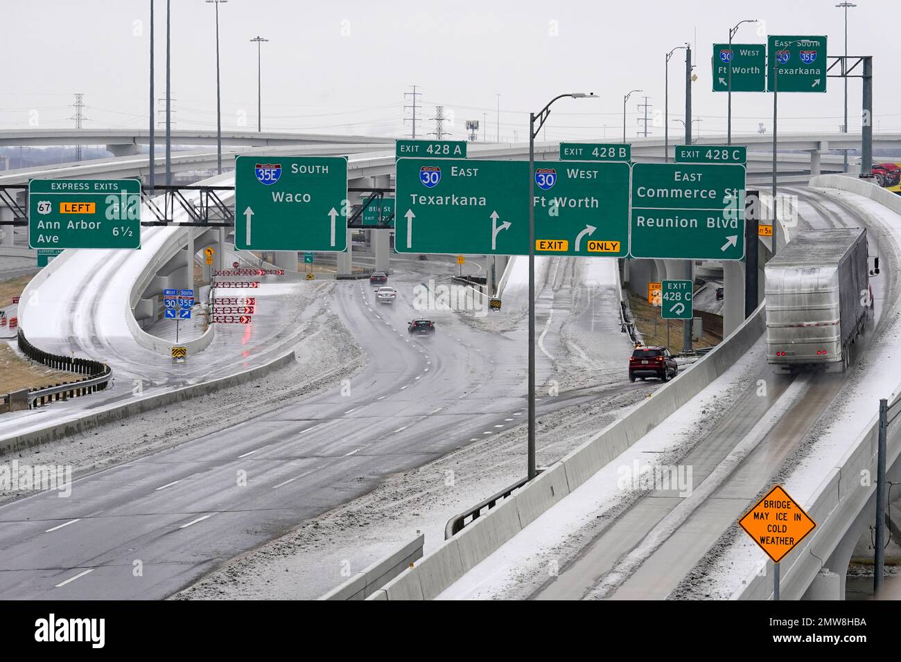 A road sign in yellow warns drivers of icy road conditions at a busy IH 30 and IH 35 interchange ...