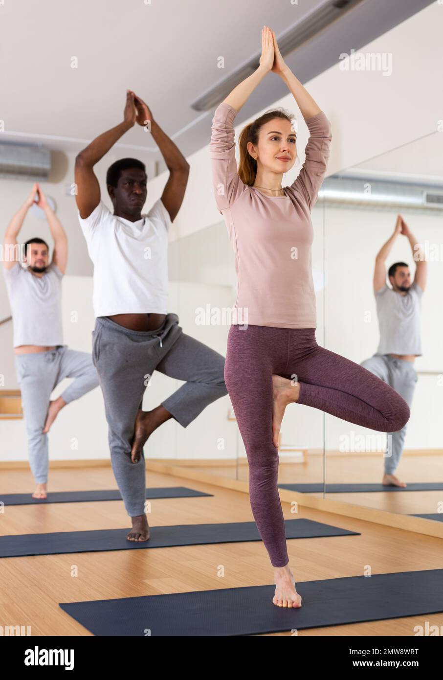 Woman doing balancing asana Vrikshasana during group yoga class Stock ...