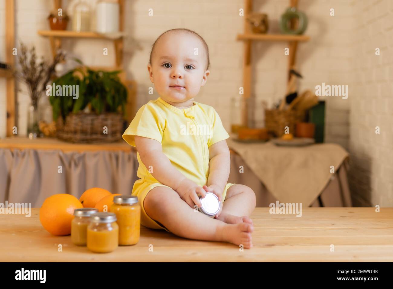 a cute kid in a yellow bodysuit is sitting in the kitchen with cans of ...