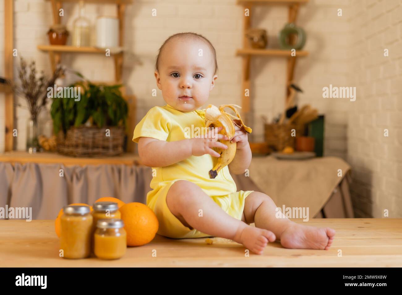 a cute kid in a yellow bodysuit is sitting in the kitchen with cans of ...