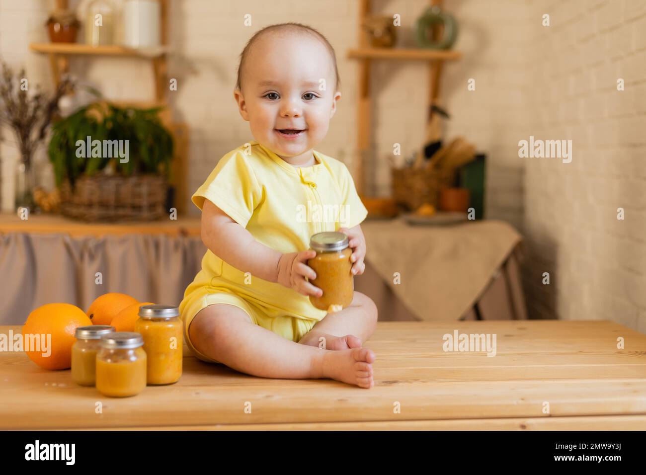a cute kid in a yellow bodysuit is sitting in the kitchen with cans of ...