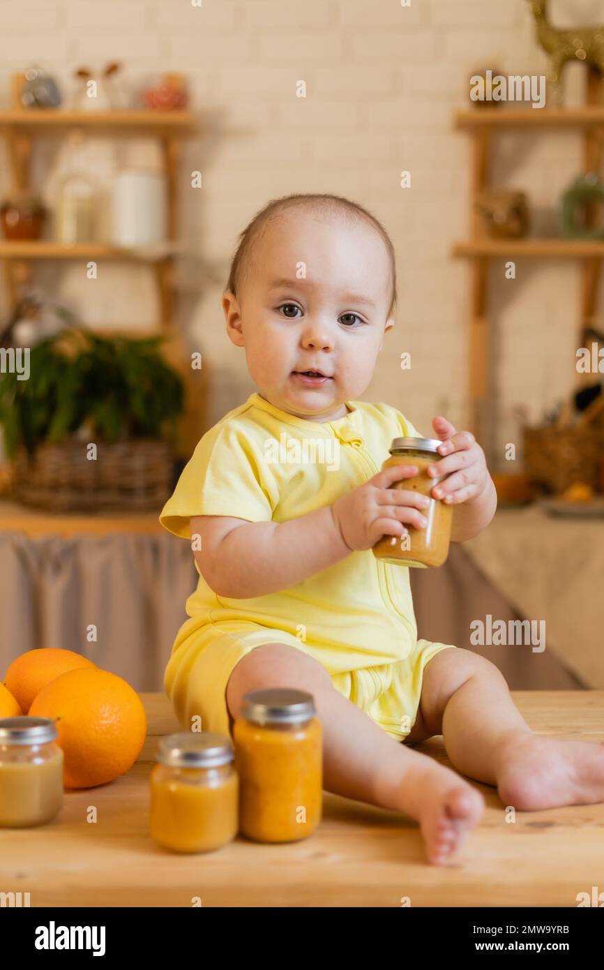 a cute kid in a yellow bodysuit is sitting in the kitchen with cans of ...