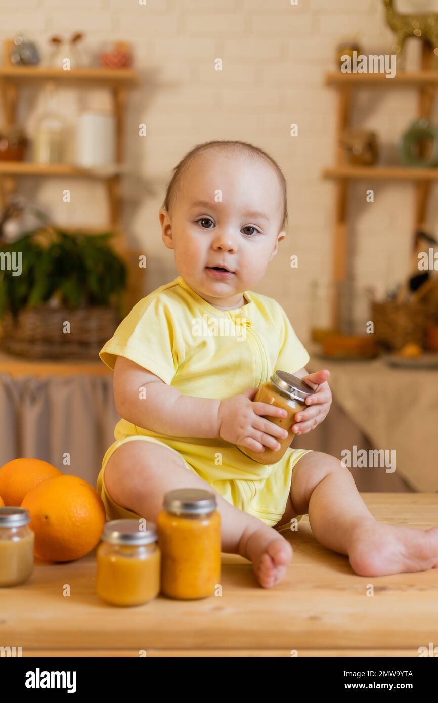 a cute kid in a yellow bodysuit is sitting in the kitchen with cans of ...