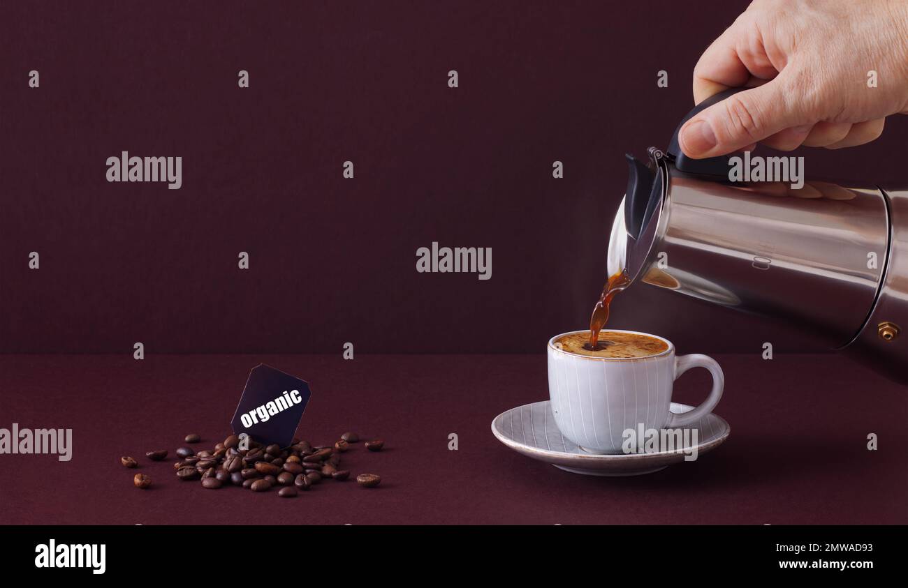 A hand pouring coffee from a mocha pot into a small cup next to a pile ...