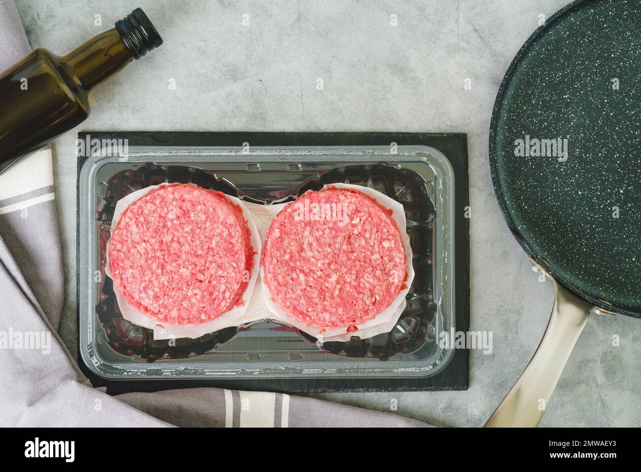 Burger patties in plastic conteiner, olive oil, and frying pan close-up ...