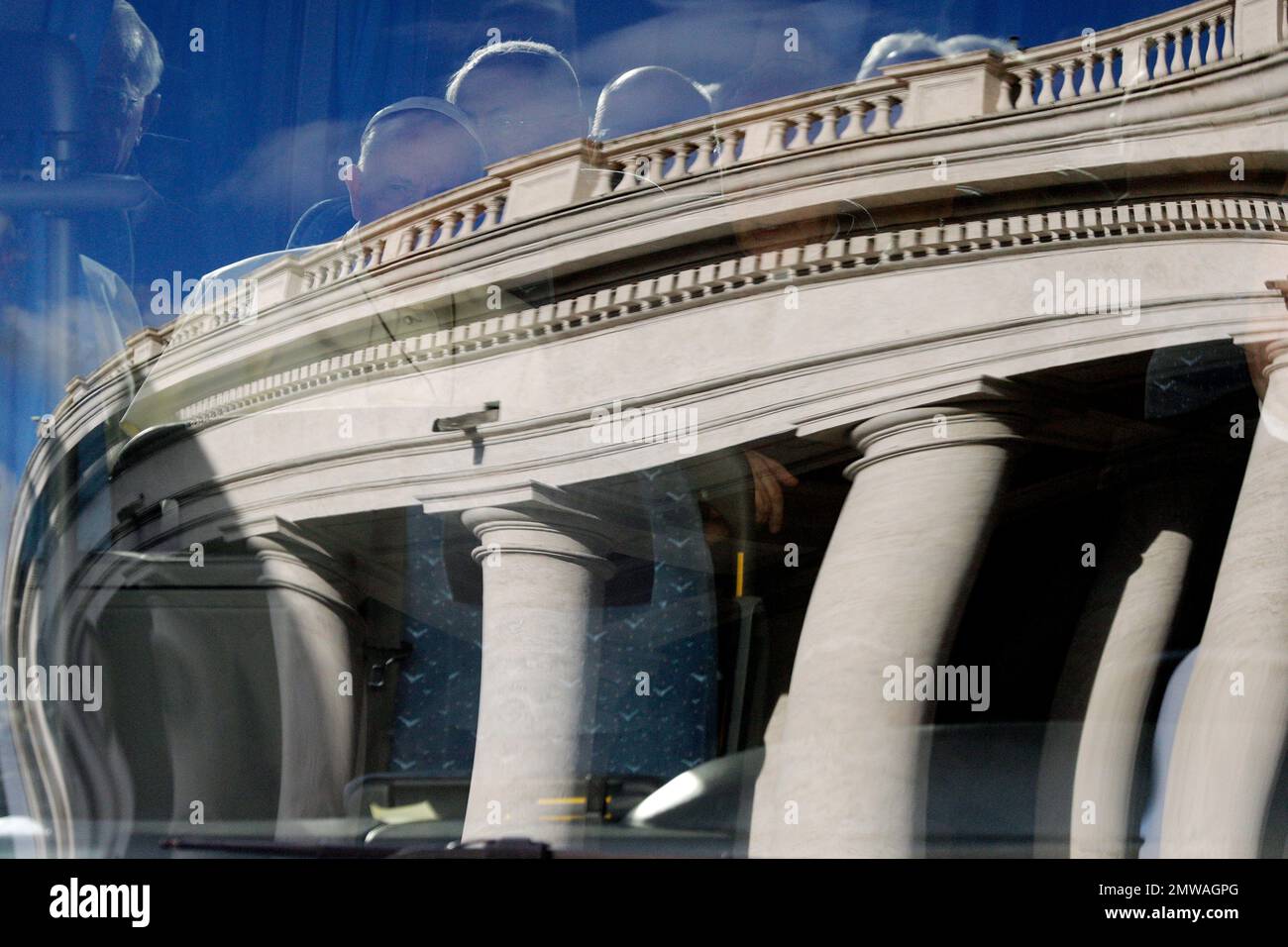Pope Francis, left, sits on a bus as the Bernini colonnade is reflected ...