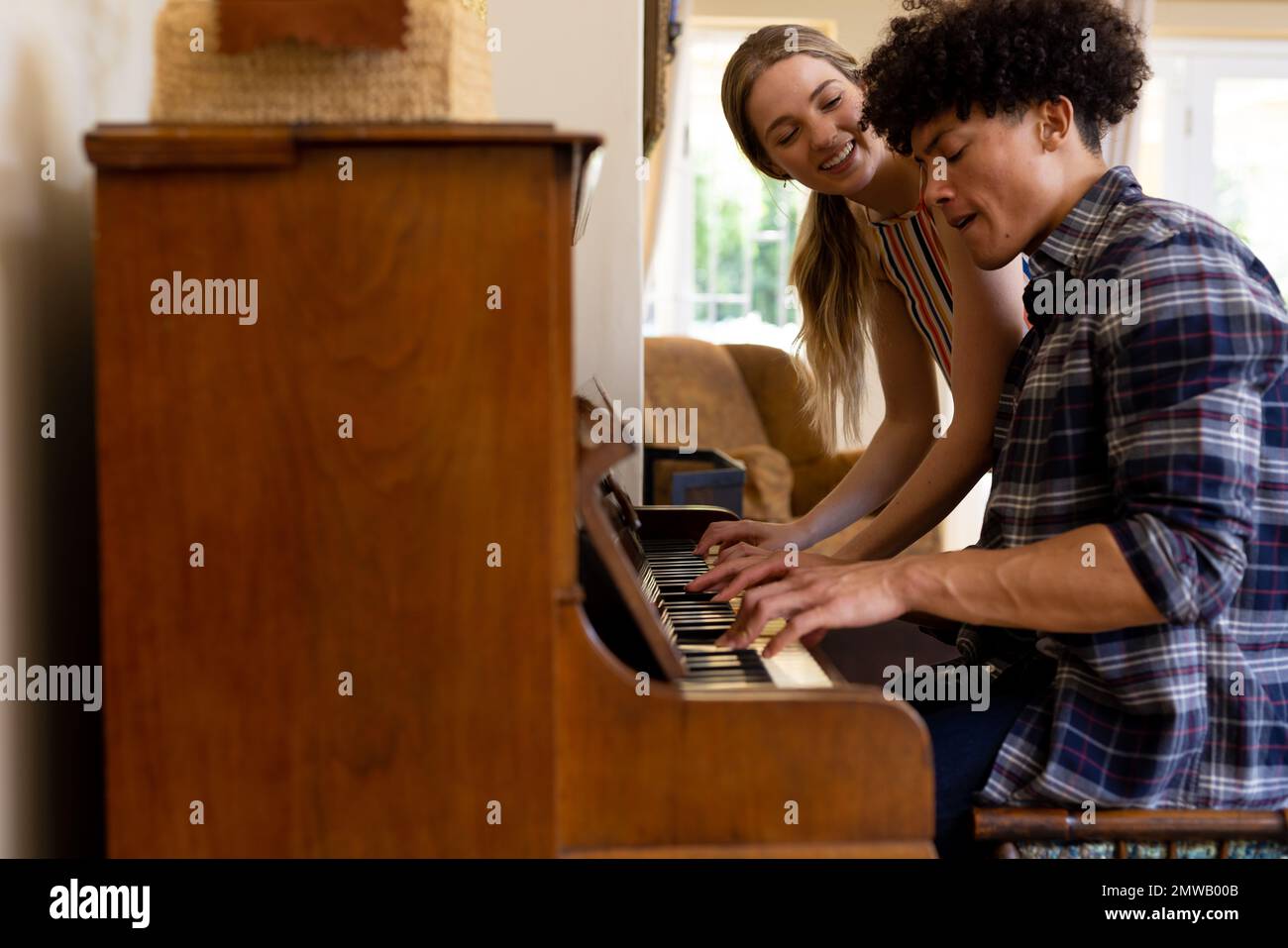 Happy diverse couple having fun playing piano together at home, copy ...