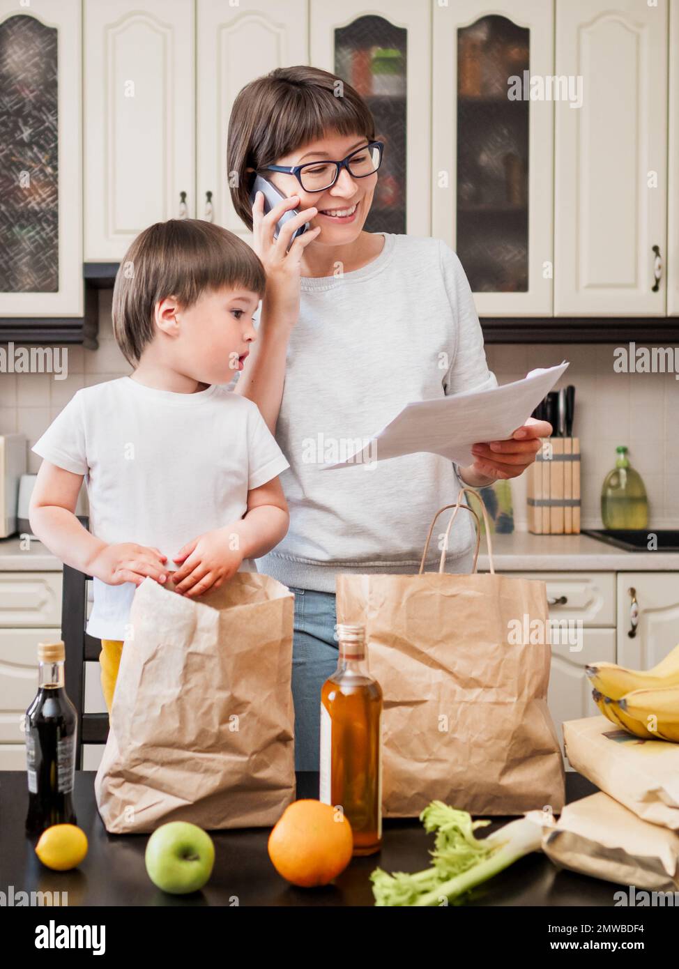 Woman and toddler boy sort purchases in kitchen. Grocery delivery in ...