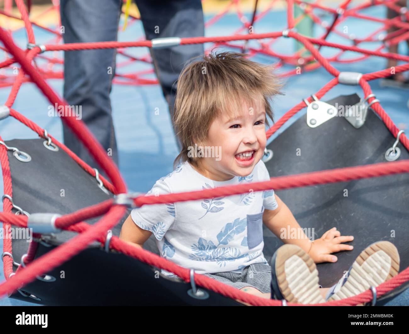 Laughing toddler is jumping on playground. Outdoor sport equipment for ...