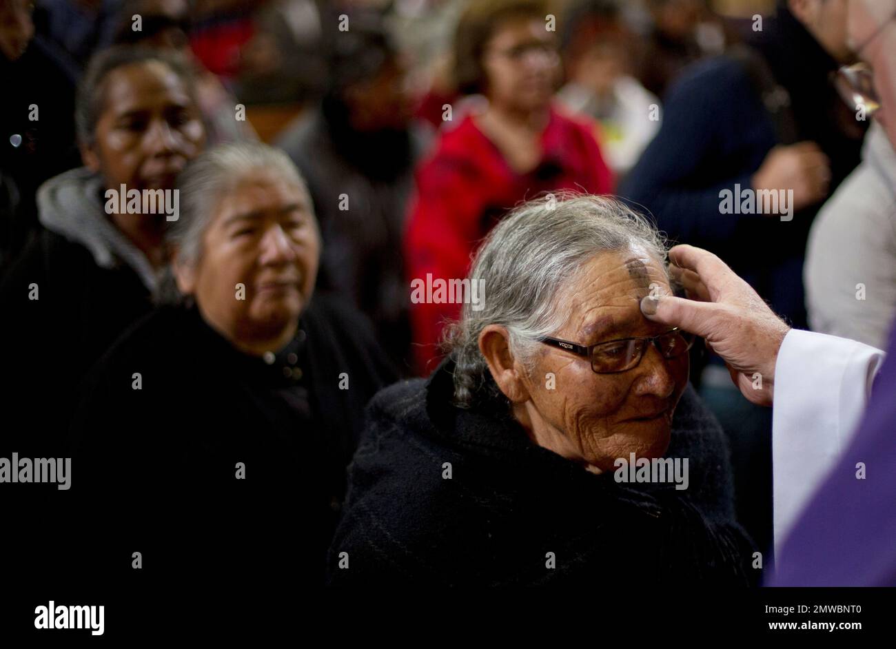A Catholic priest marks the symbol of the cross on a woman's forehead ...