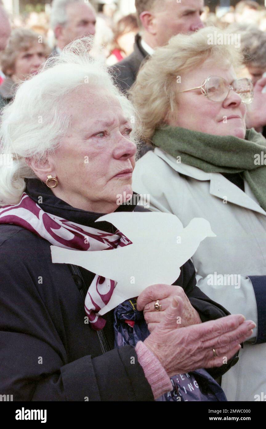 An elderly lady fights back the tears clutching a paper dove of peace ...