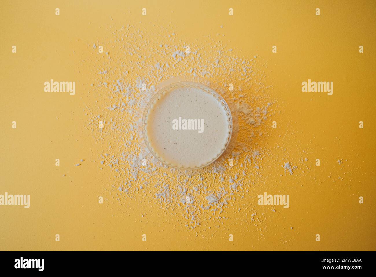 A plastic bowl of creamy pudding on a yellow background with spilled ...