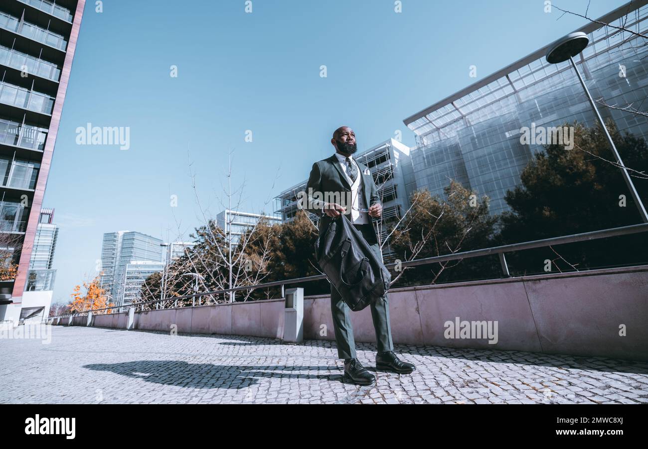 An elegant African executive male standing on the sidewalk, dressed in ...