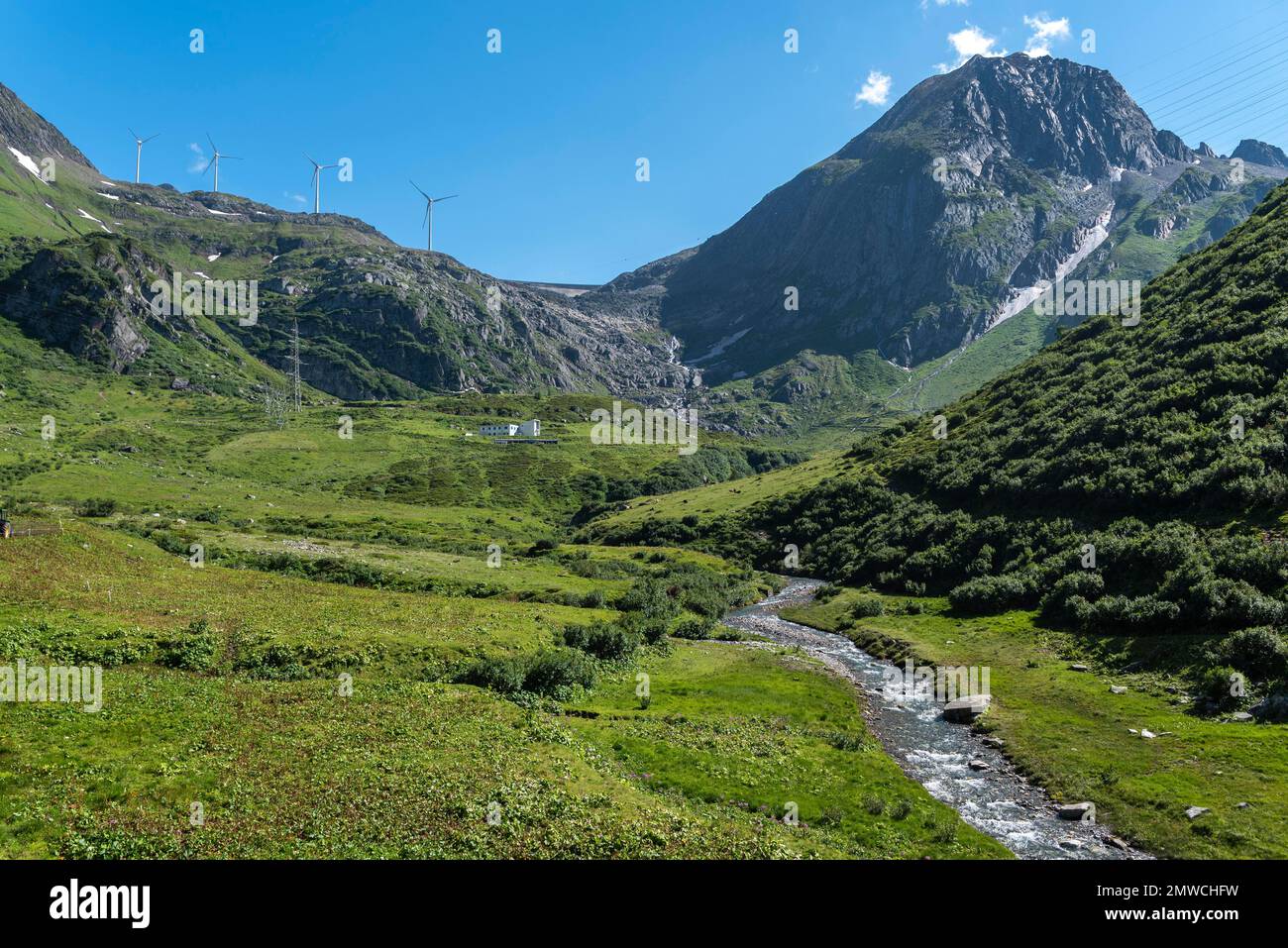 Alpine landscape along the Nufenen Pass road with wind turbine below ...