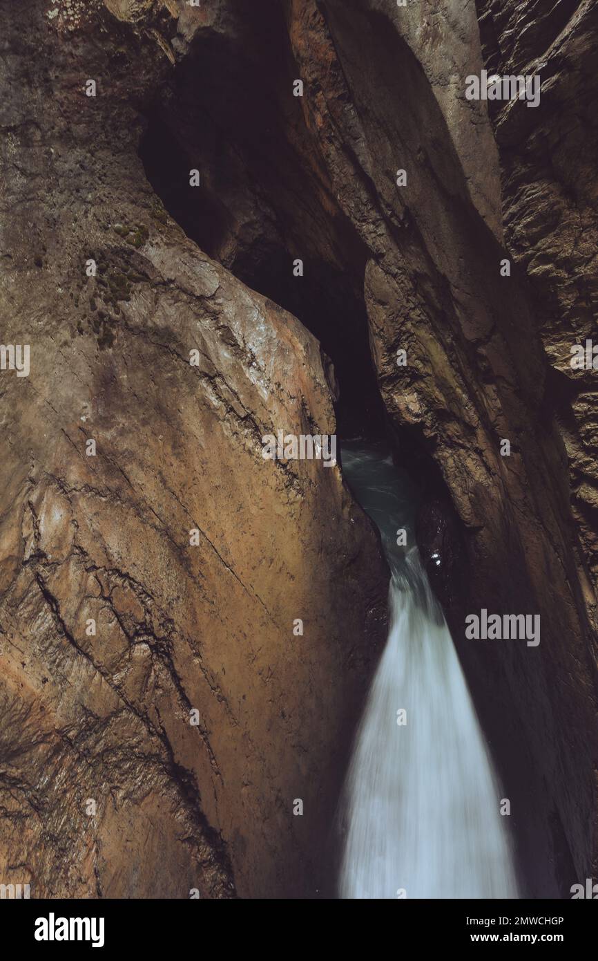 A vertical long exposure shot of a waterfall flowing from a cave in a ...