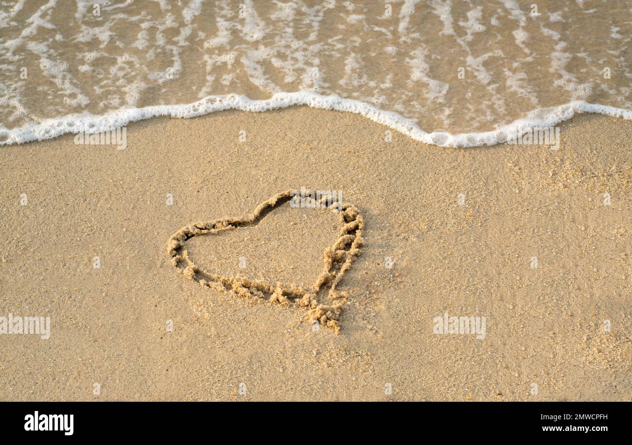 Heart shape on the sand of a beach with wave foam at the background ...