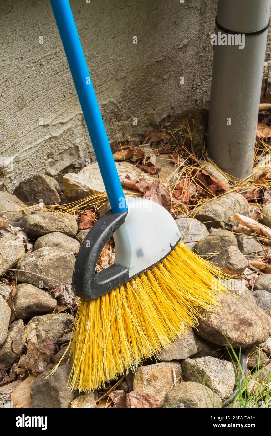 Broom in rock border leaning against exterior wall of house, Quebec ...