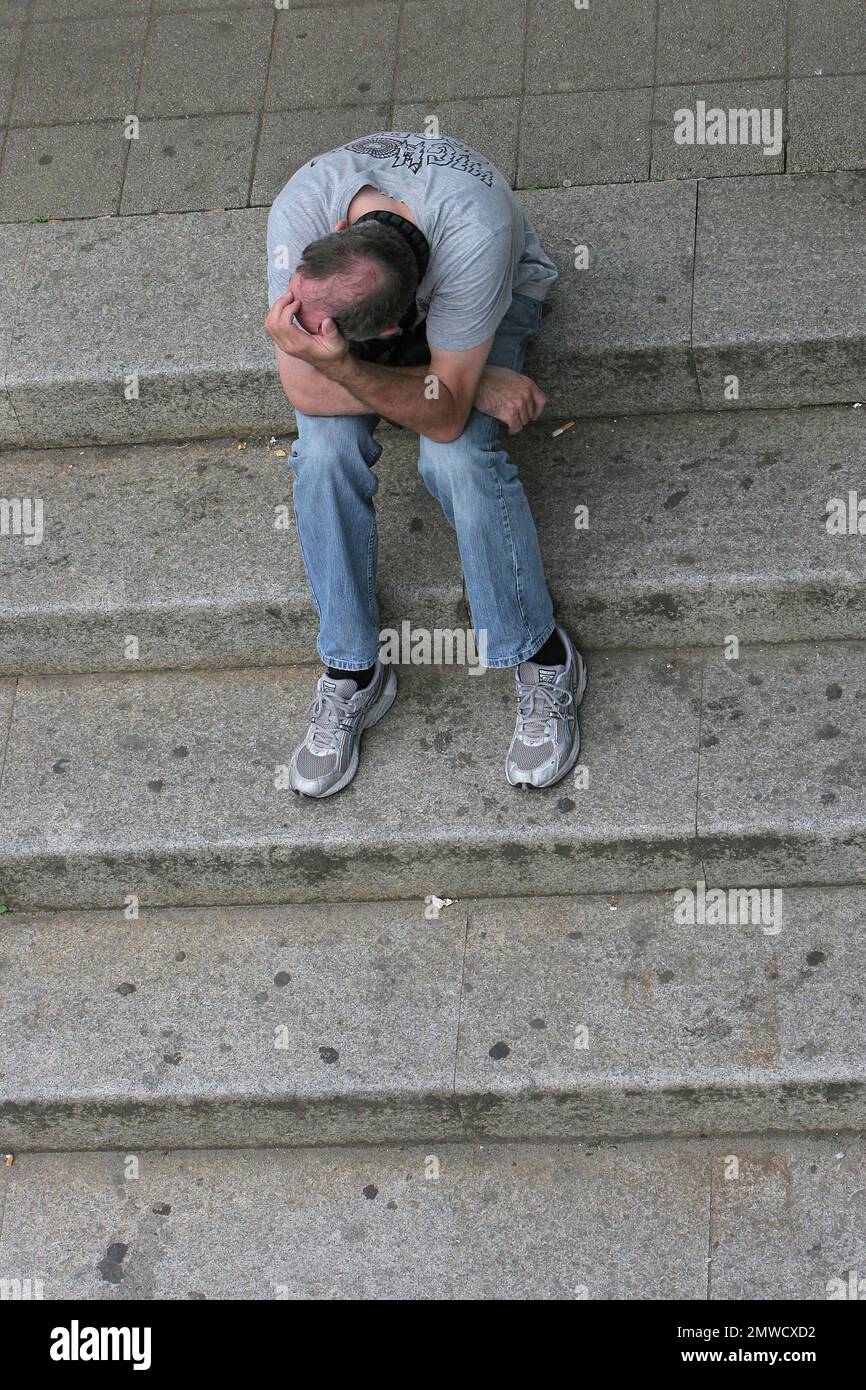 Desperate-looking man sits on stairs with arms propped up, desperation ...