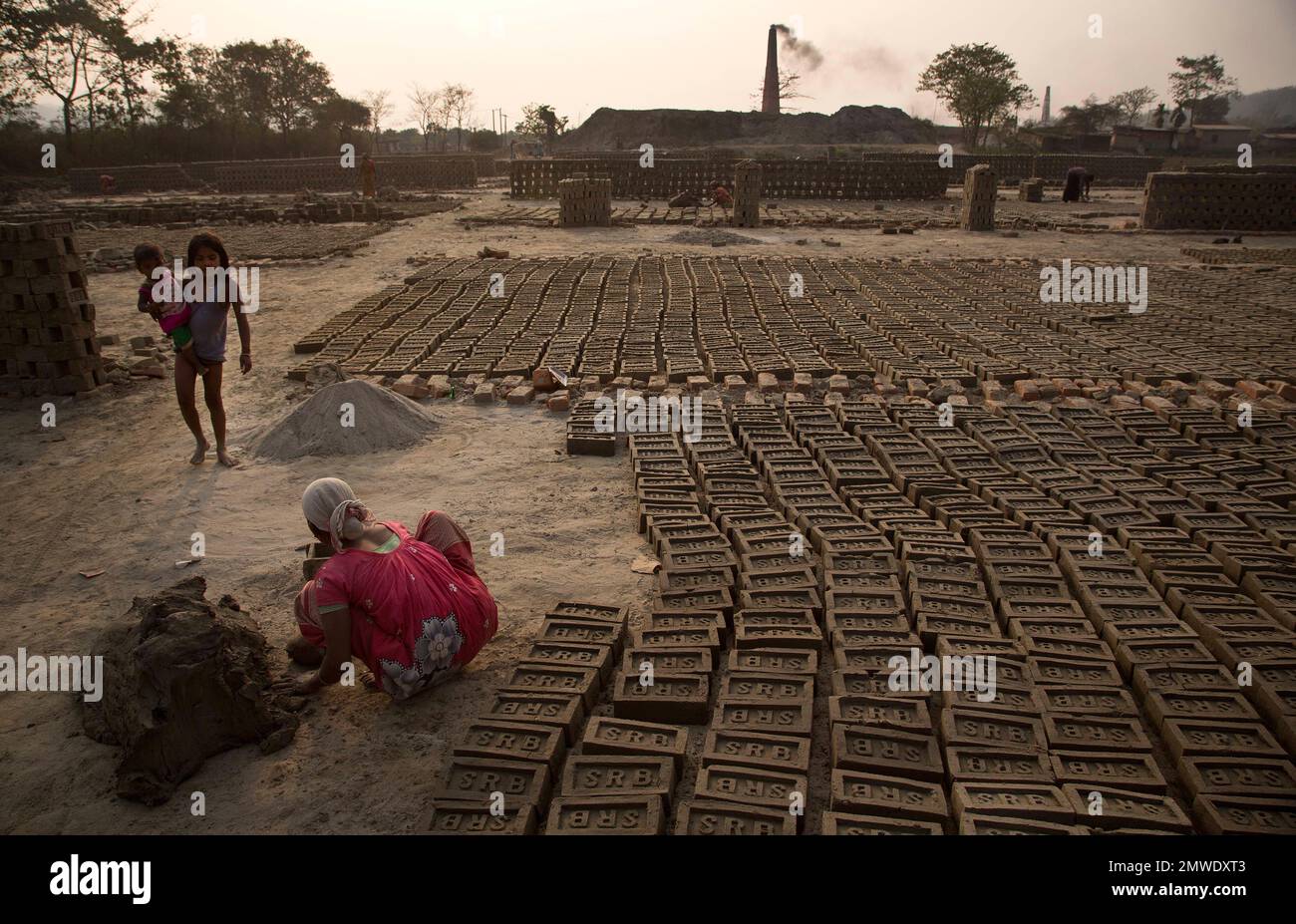 An Indian child carries an infant as a woman makes bricks at a brick ...