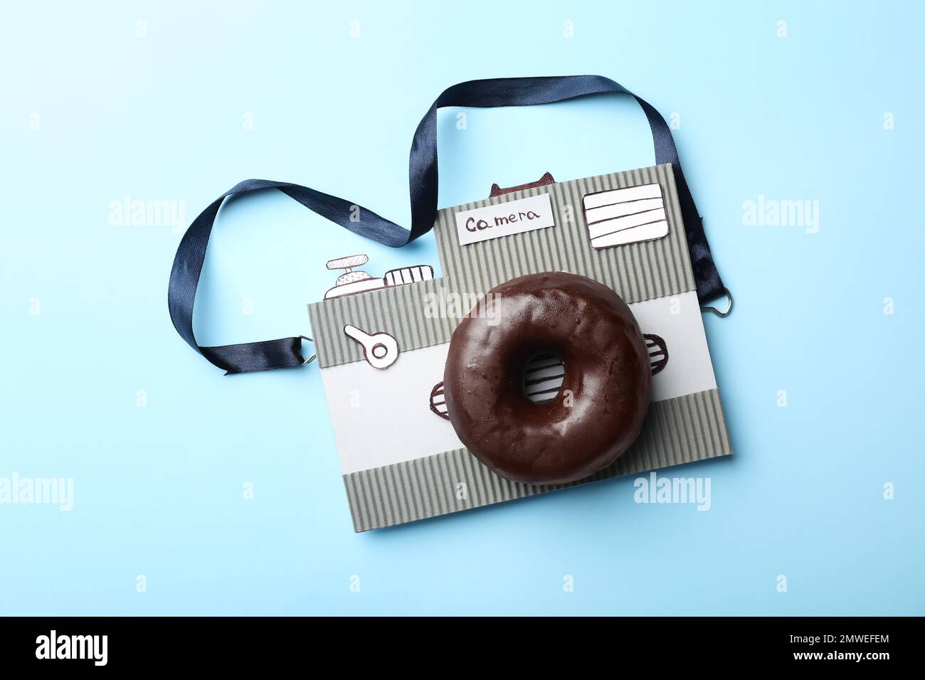 Camera made from donut and piece of cardboard on light blue background ...