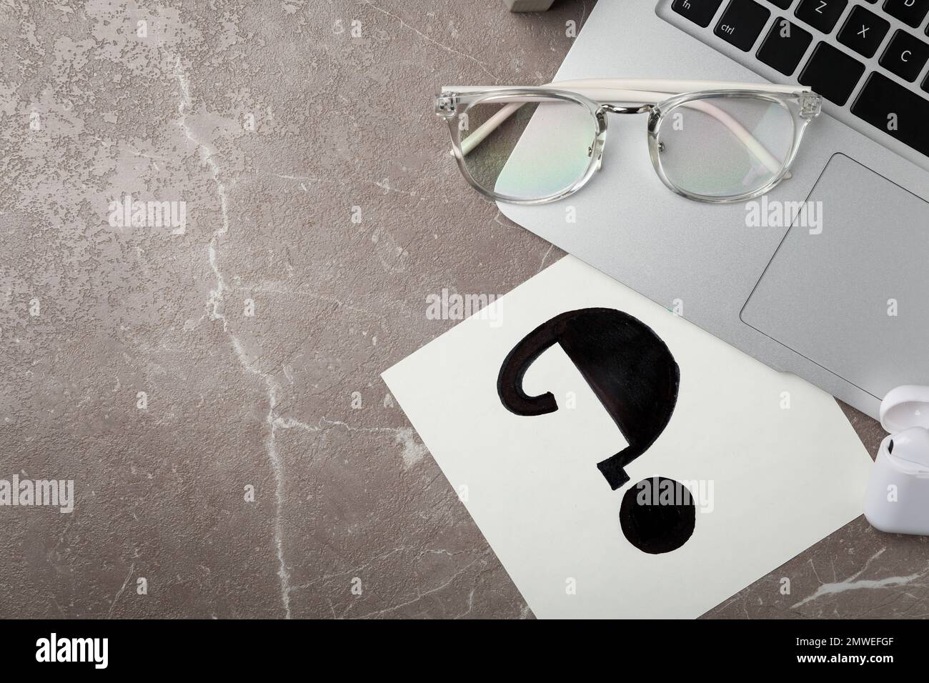 Notebook with question mark, laptop and eyeglasses on grey marble table ...