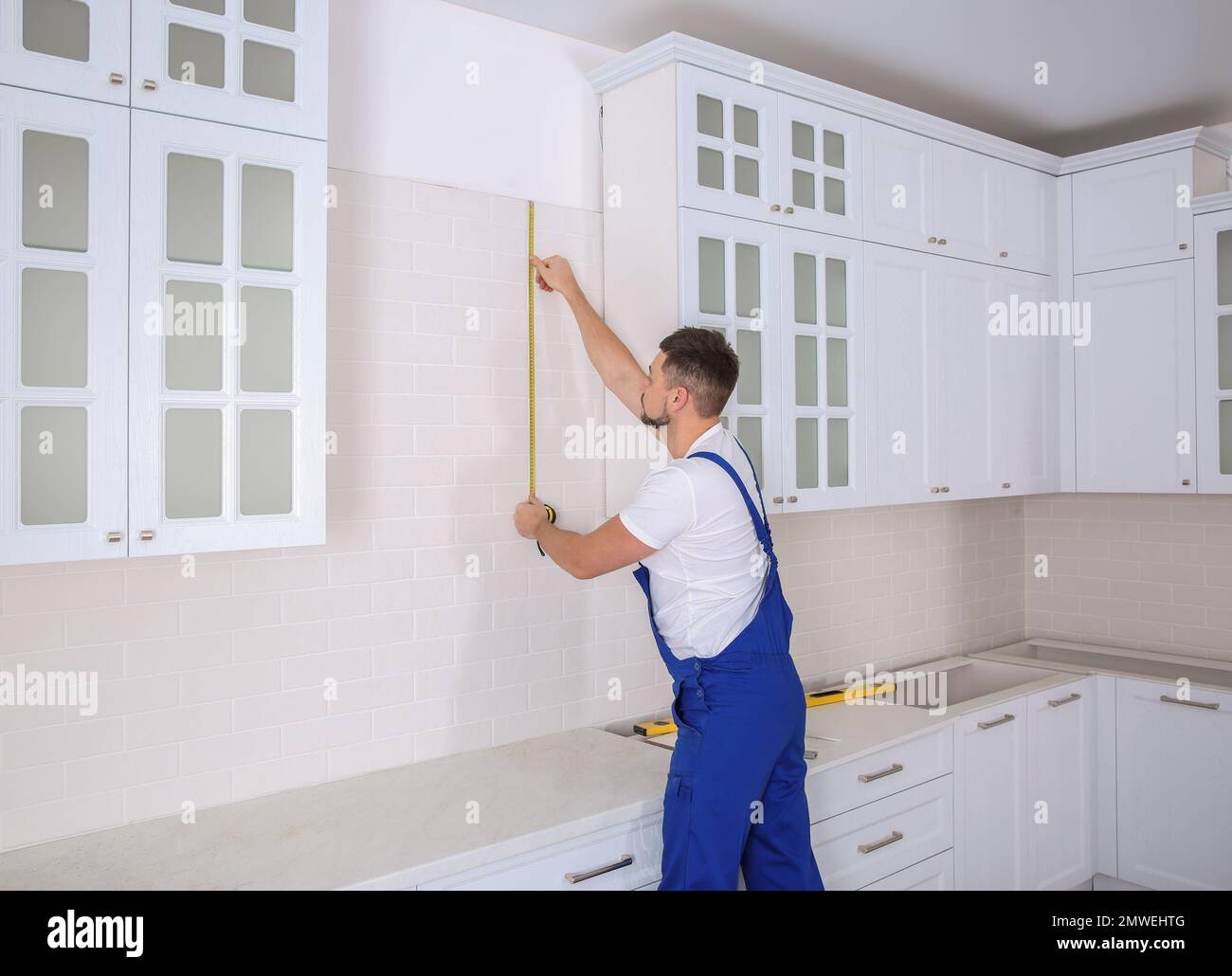 Worker using measuring tape while installing new furniture in kitchen ...
