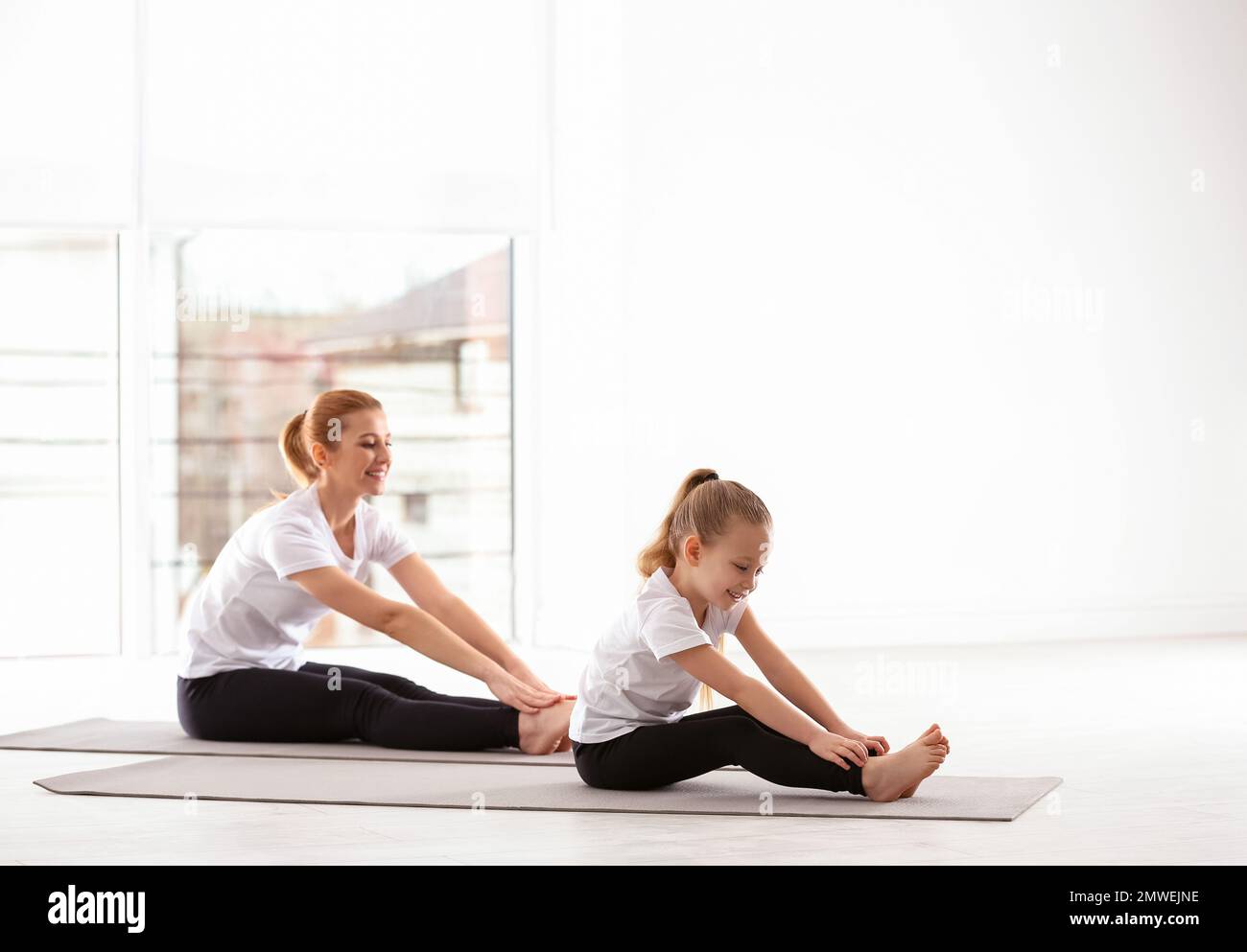 Mother and daughter in matching sportswear doing yoga together at home ...