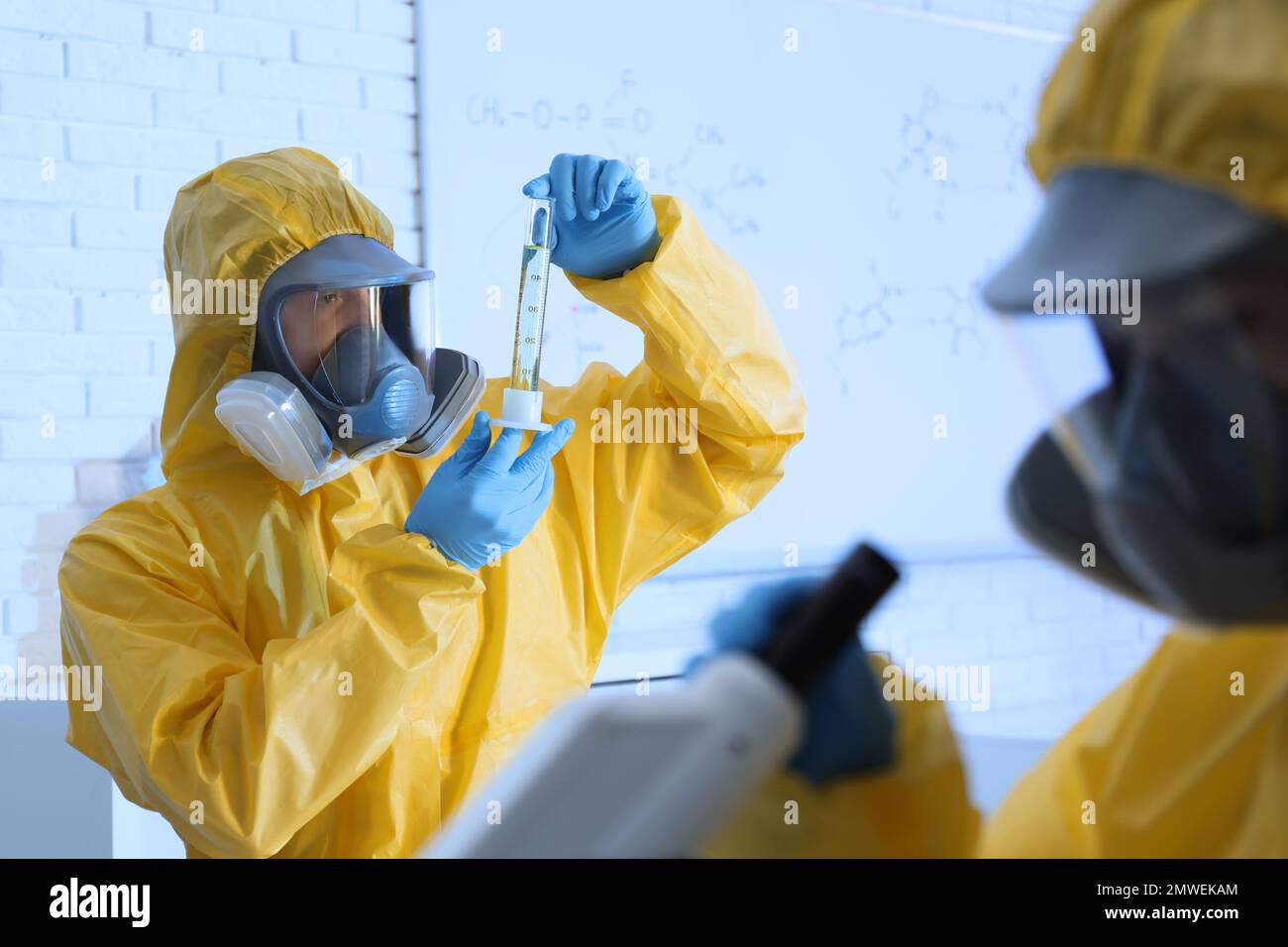 Scientist in chemical protective suit with graduated cylinder at ...