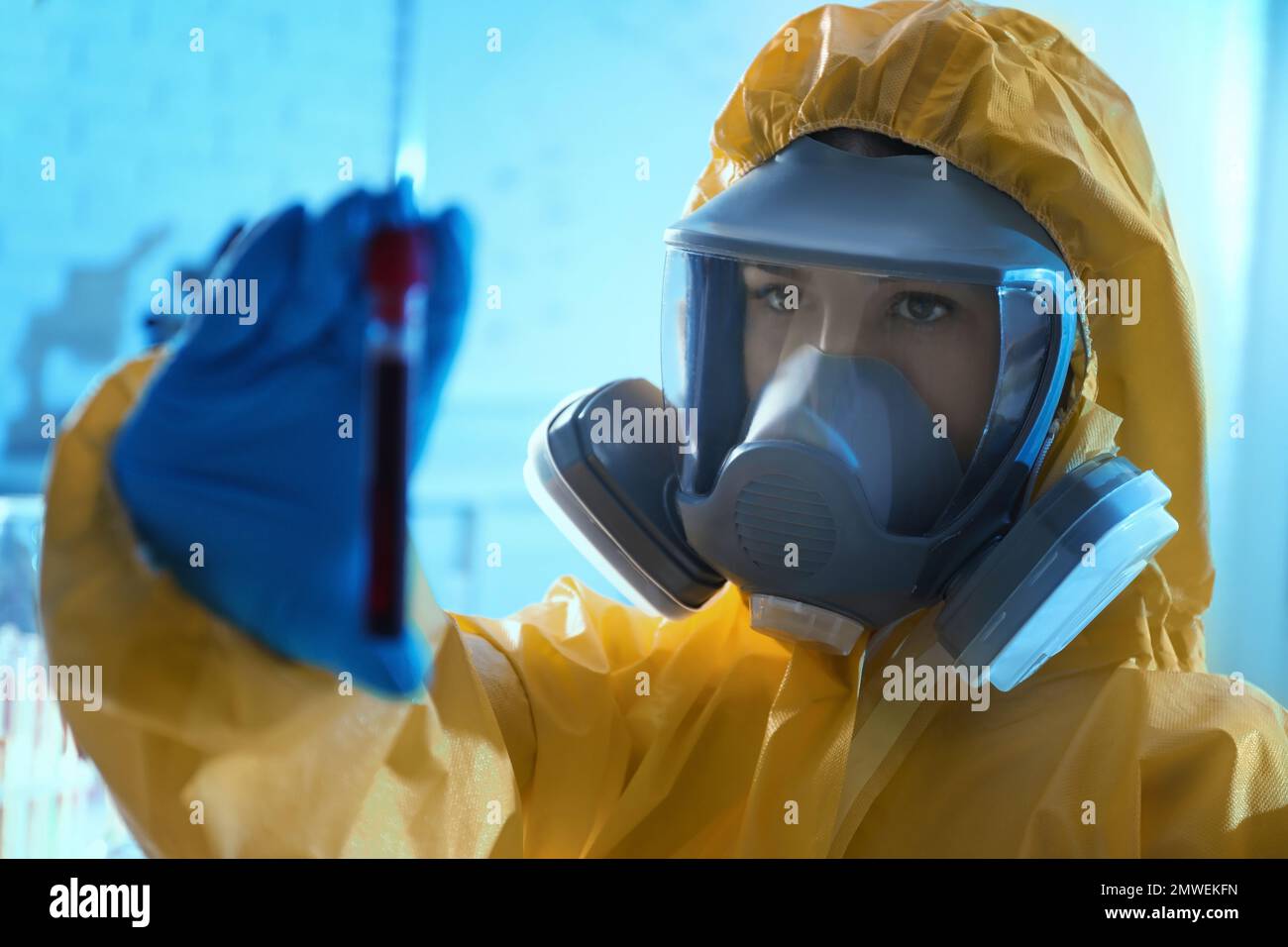 Scientist in chemical protective suit holding test tube with blood ...
