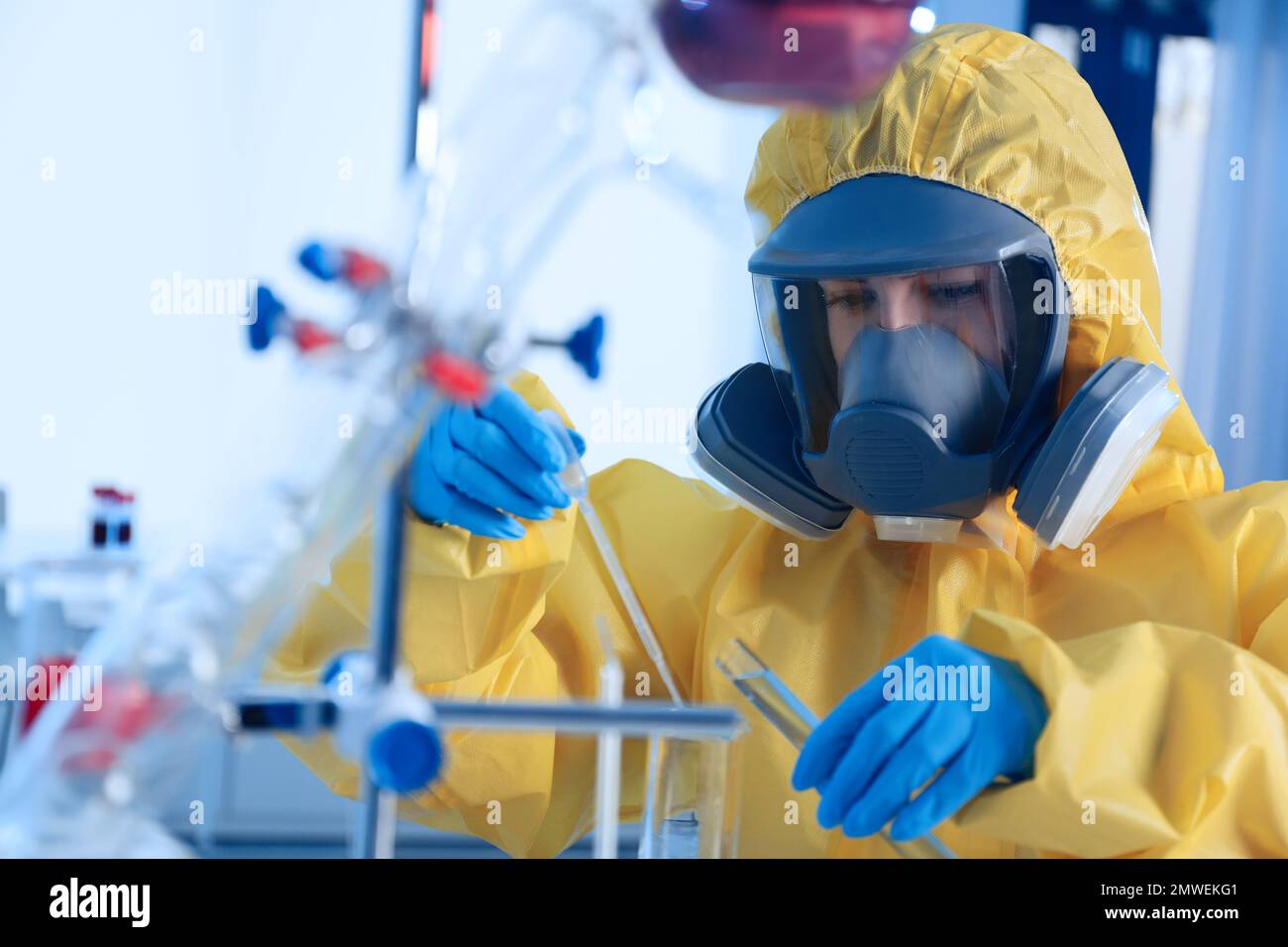 Scientist in chemical protective suit dripping reagent into test tube ...