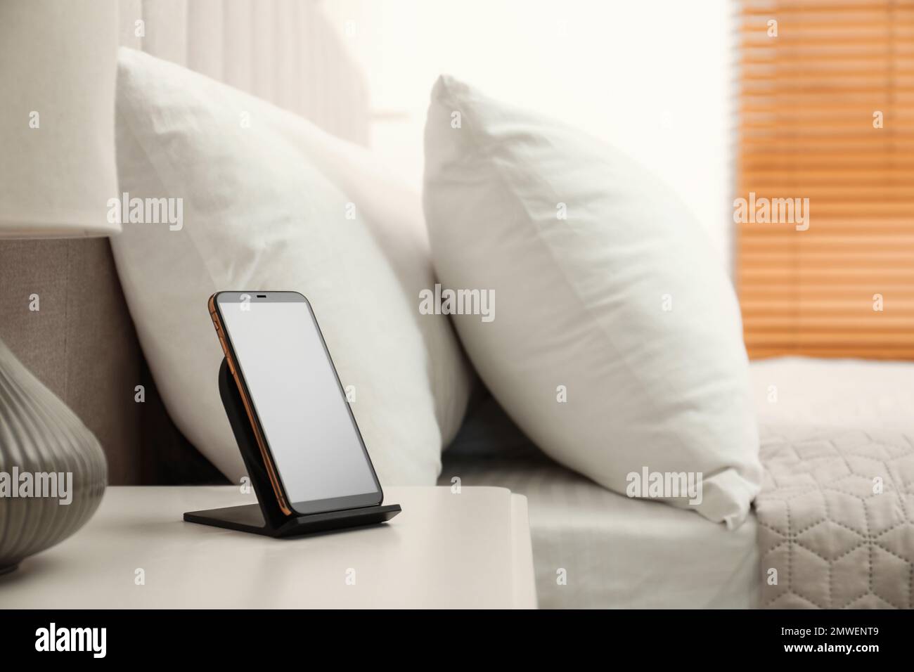 Modern mobile phone charging on wireless pad in bedroom. Space for text ...