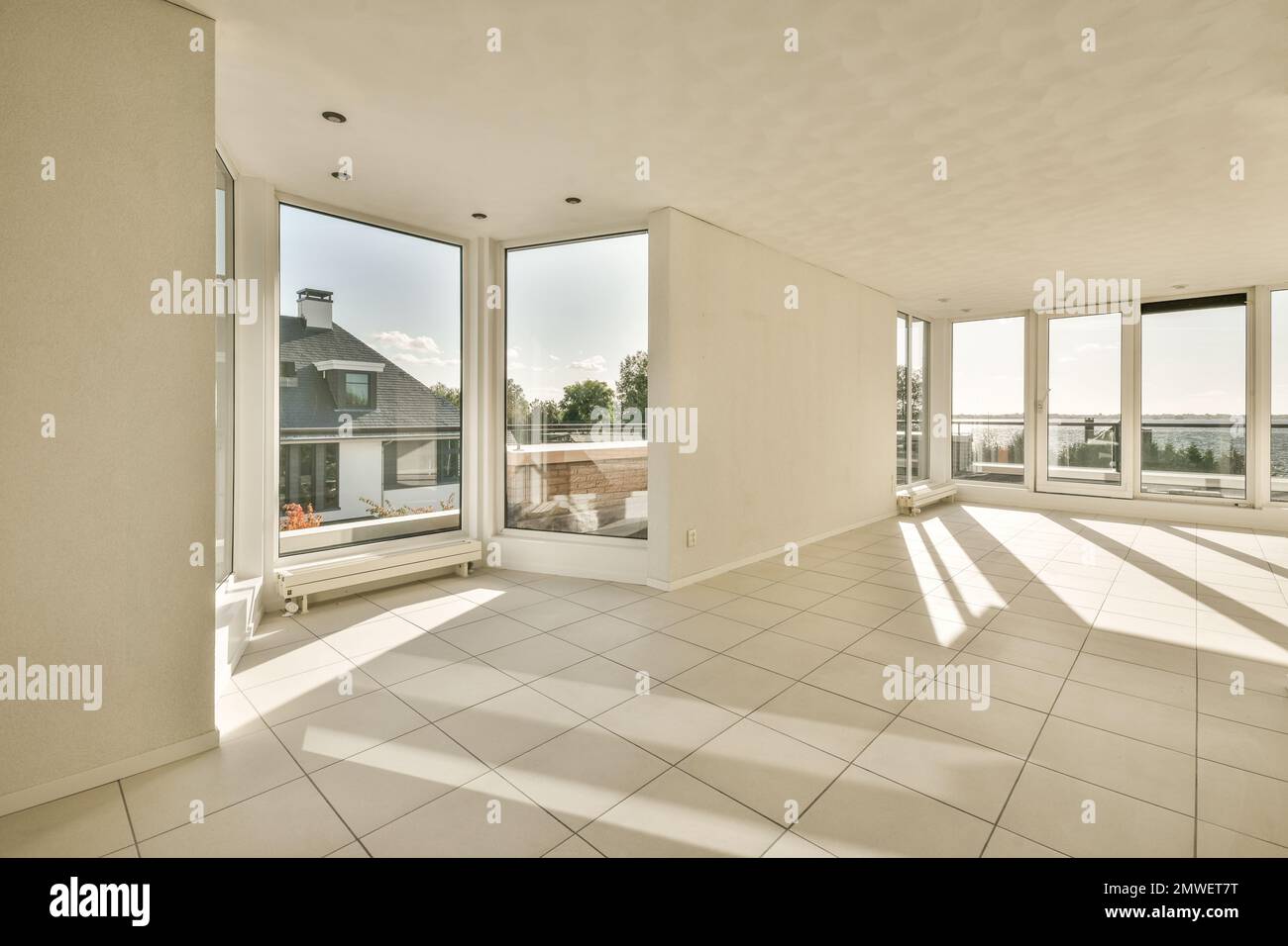 an empty room with white tile flooring and large windows that look out ...