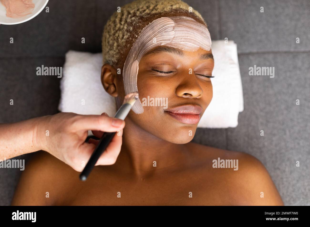 Hand of beautician giving facial to smiling african american woman with ...