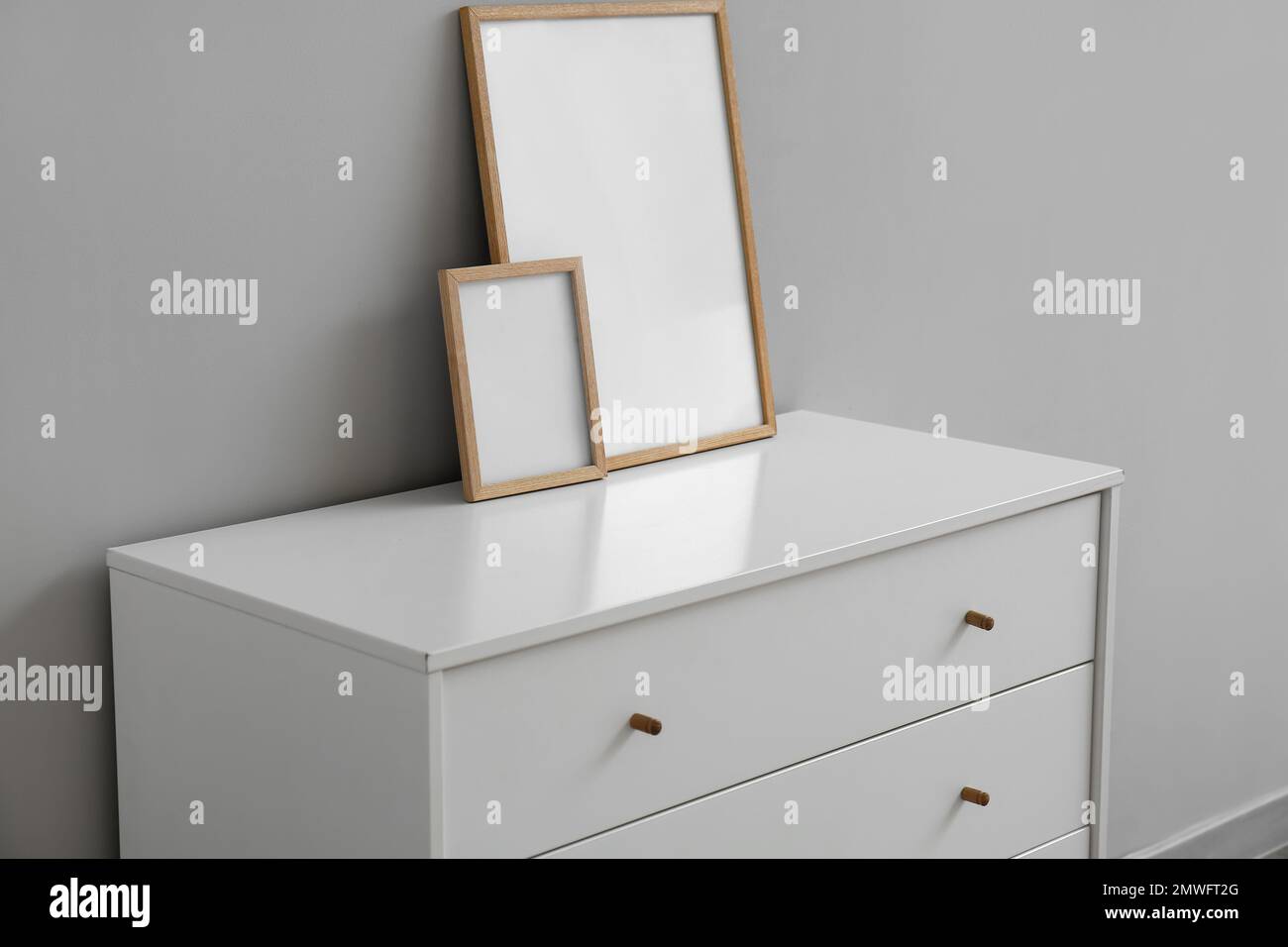 White chest of drawers with blank frames near grey wall Stock Photo - Alamy