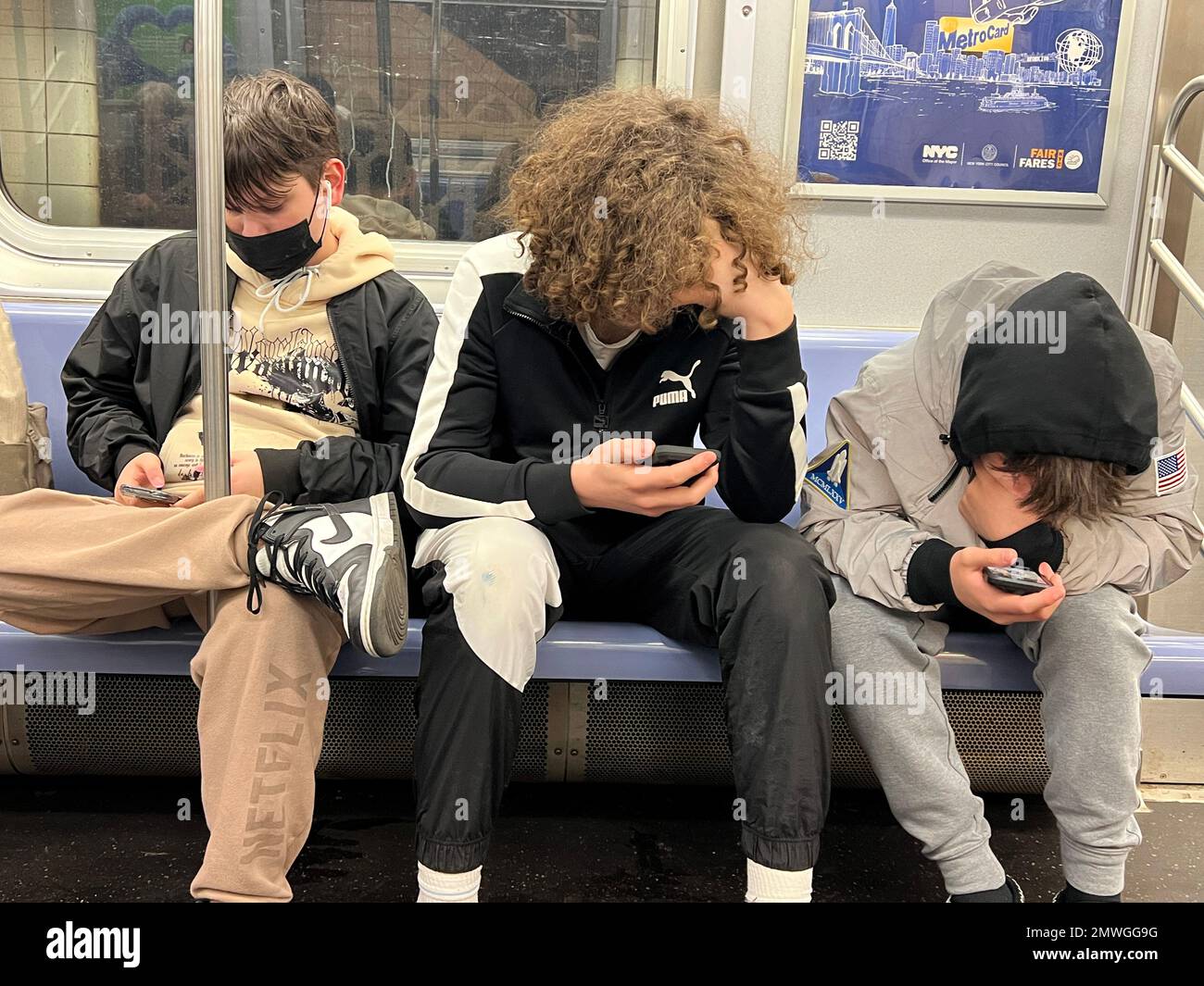 Three teenage boys doing screen time while they ride a subway train in ...