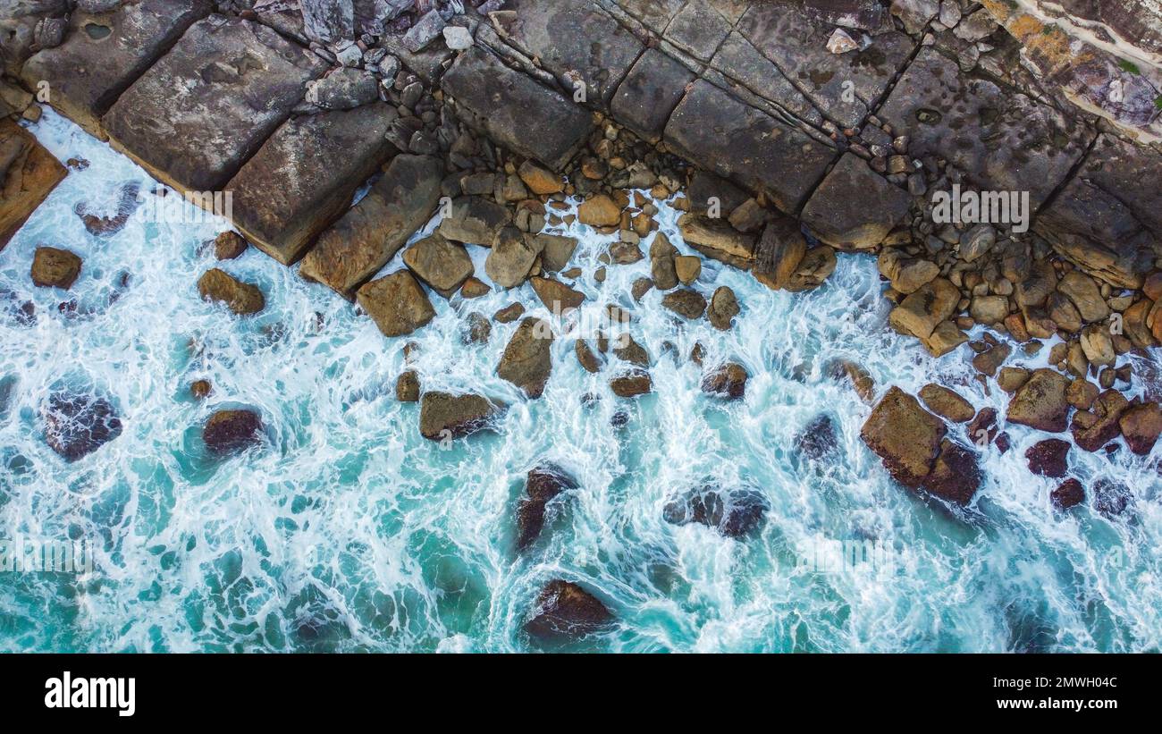 An aerial shot of a rocky coast with pieces of stones in a wavy sea ...