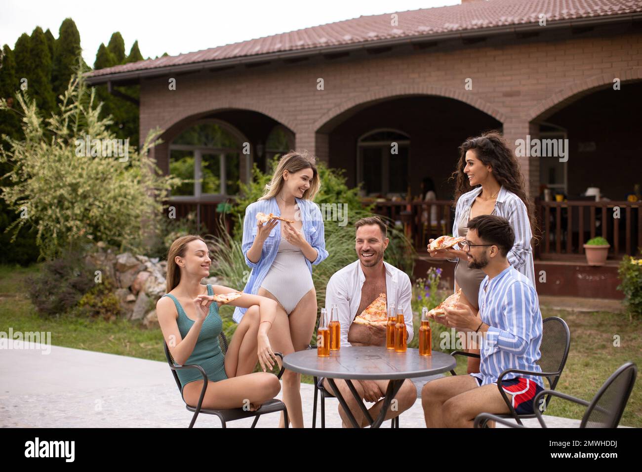 Group of happy young people cheering with cider and eating pizza by the ...