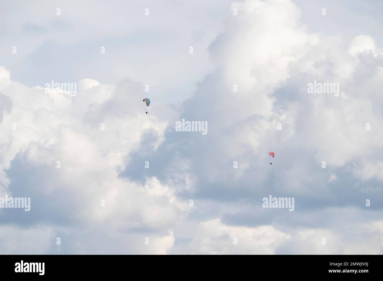 An aerial view of paragliders at a distance flying in blue cloudy sky ...