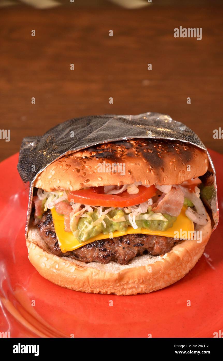 A vertical closeup of a burger wrapped in foil on a red plate in a fast ...