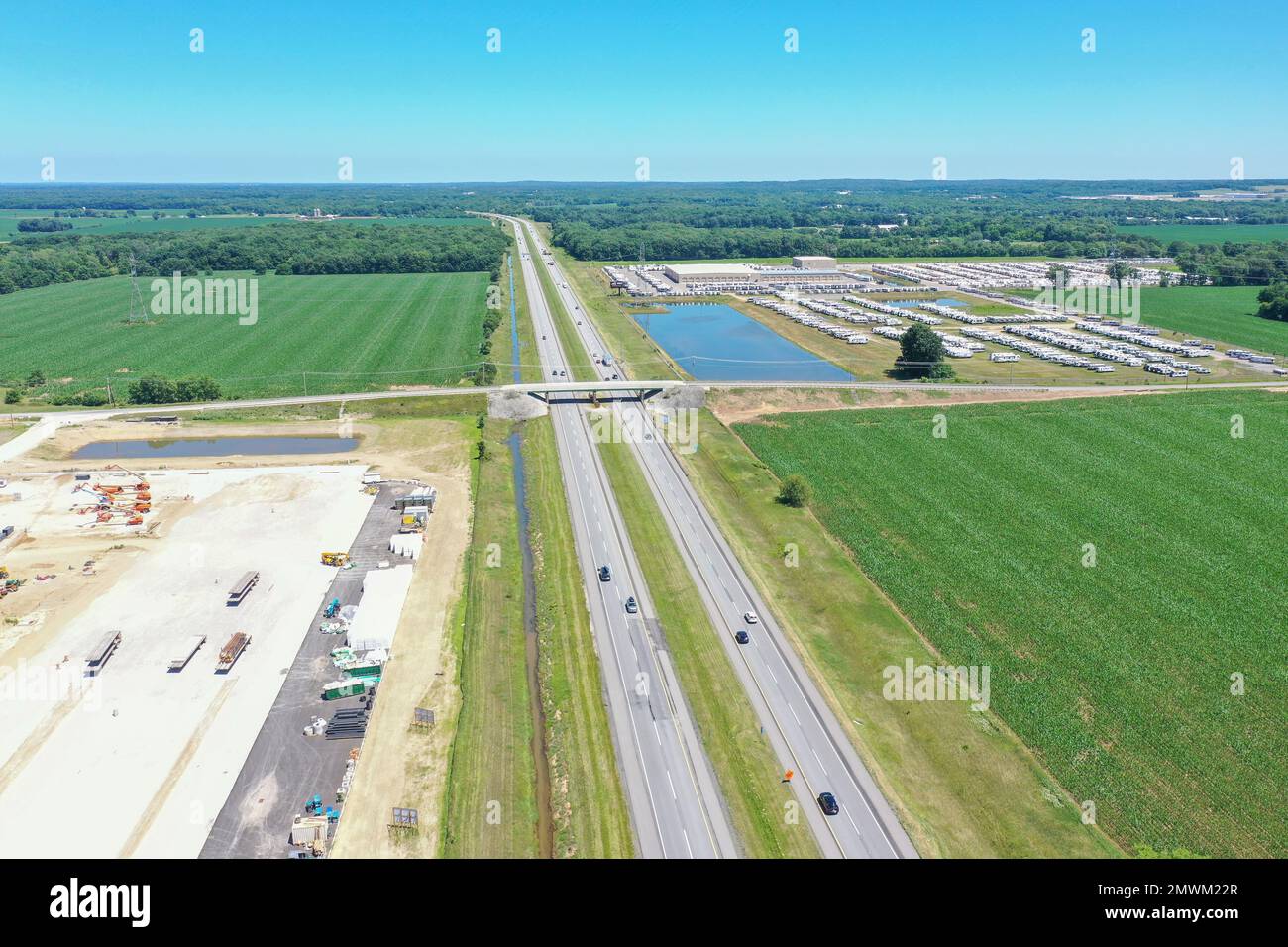 An aerial view of a highway road through a green field with a pond ...