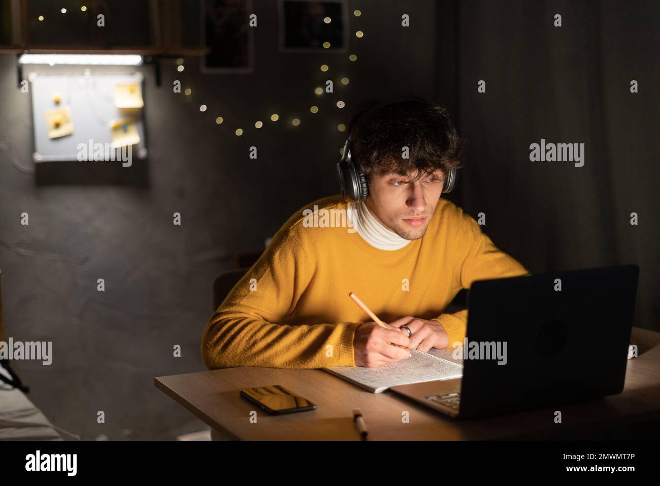 Student guy making notes in notebook using laptop computer sitting at ...