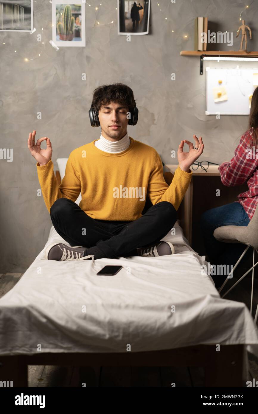 Young male university student meditating in lotus position on bed ...
