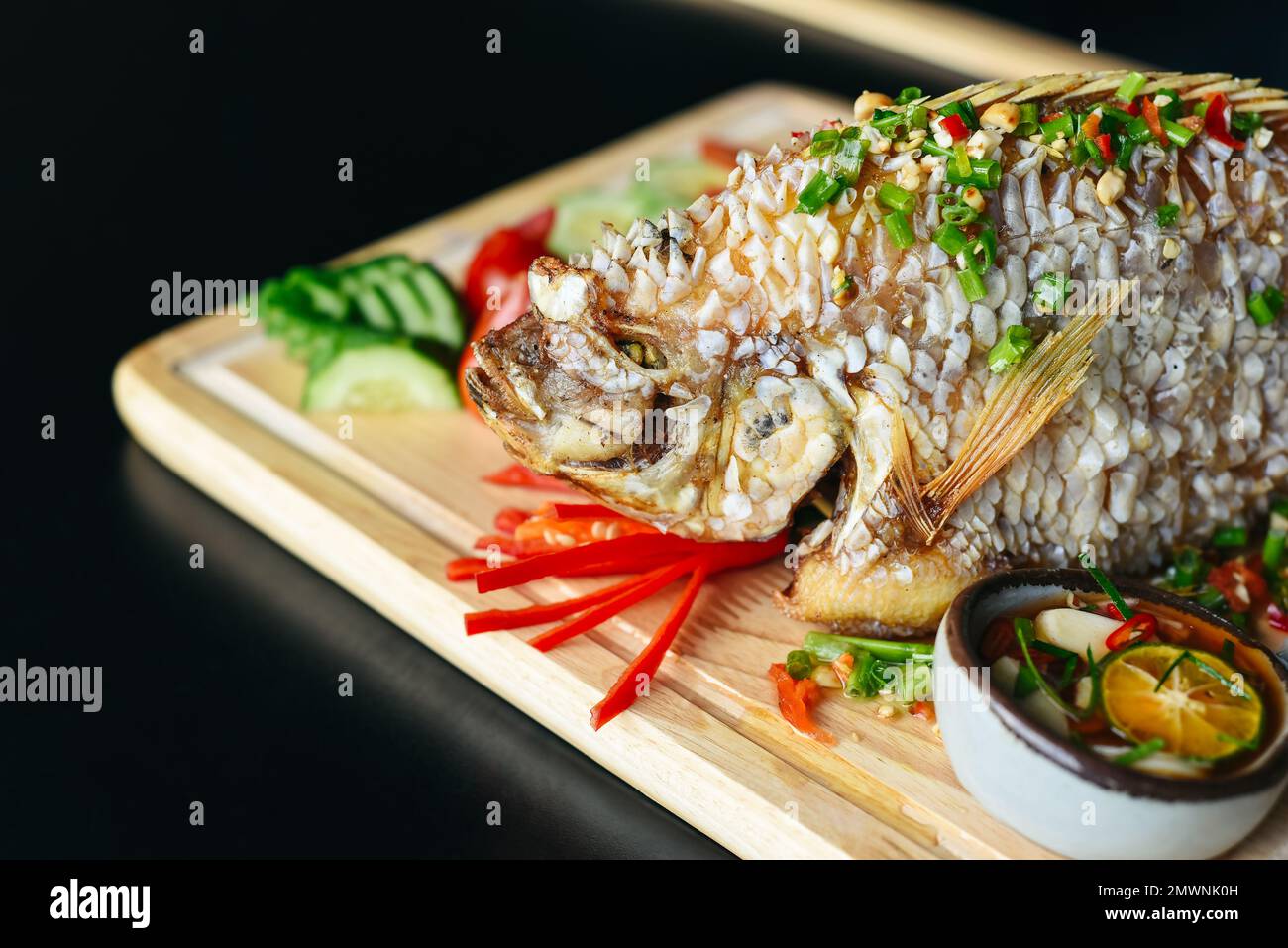 Red perch grilled in batter with vegetables and greens on wooden chop ...