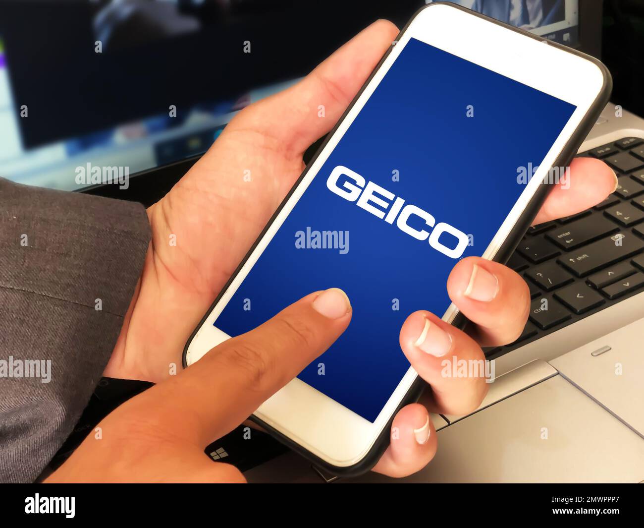 Man using Geico on Mobile with laptop in the background, editorial ...