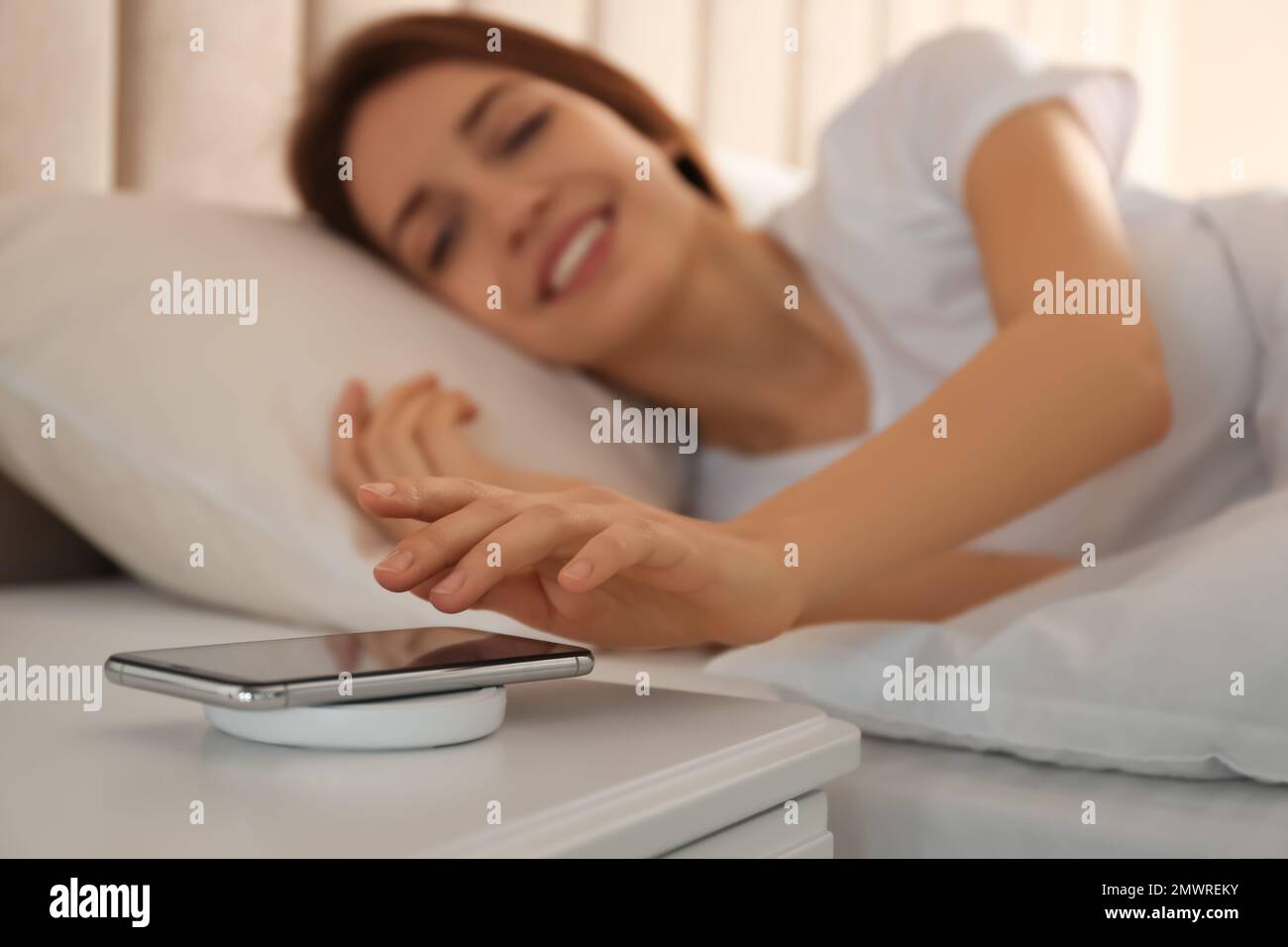 Woman taking smartphone from wireless charger in bedroom Stock Photo ...