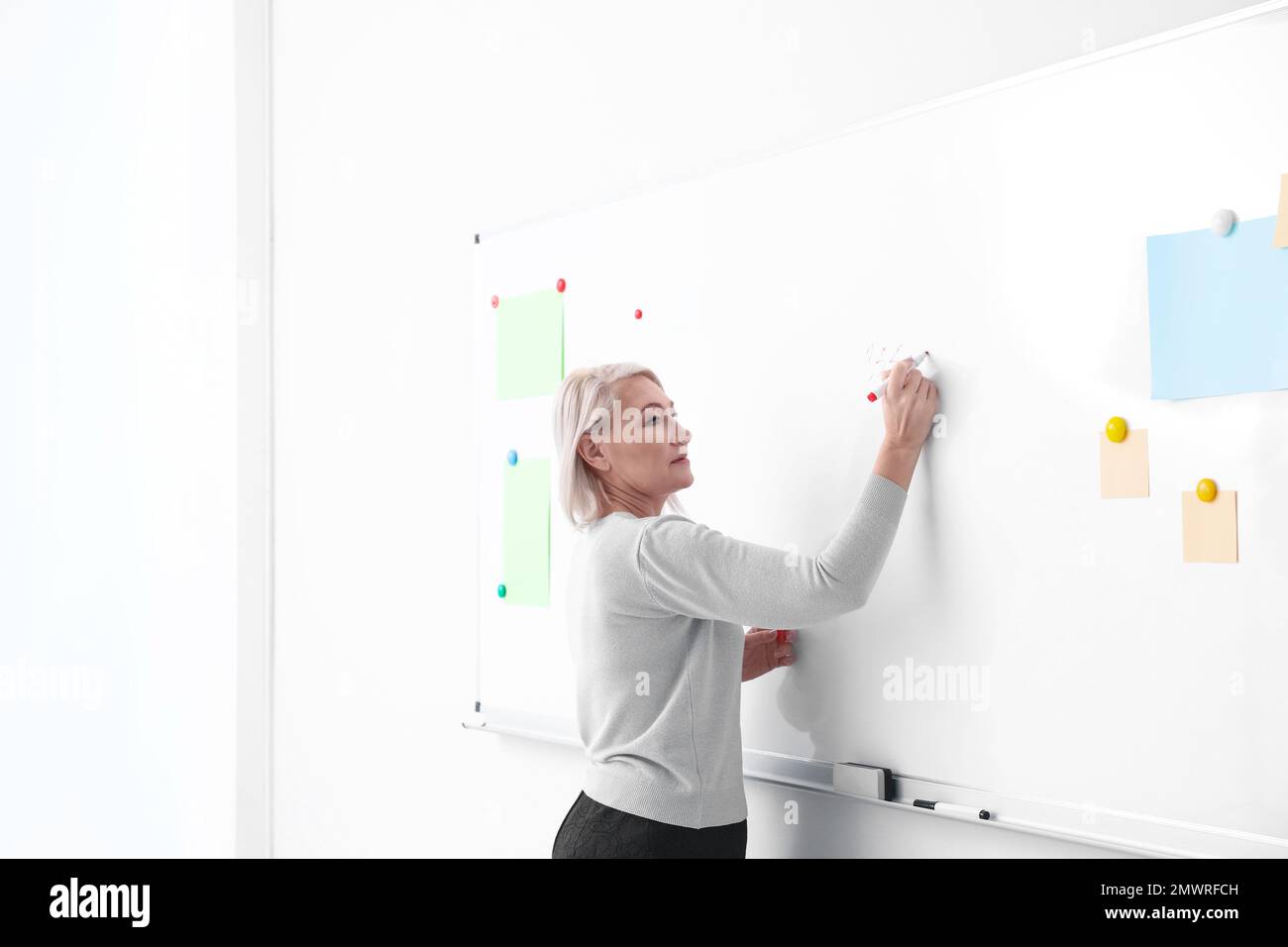 Mature teacher writing on whiteboard in classroom Stock Photo - Alamy