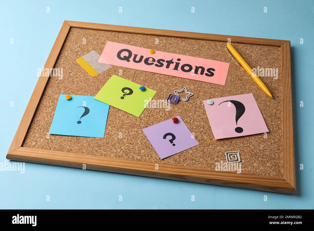 Cork board with word QUESTIONS and query marks on light blue background ...