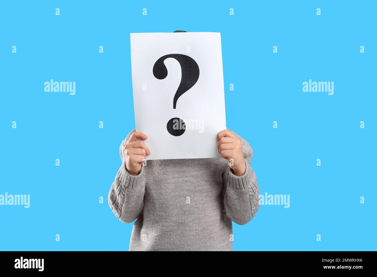 Little boy holding paper with question mark on light blue background ...
